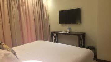 Quarto de hotel com uma cama, uma escrivaninha, uma televisão e uma janela com cortinas.