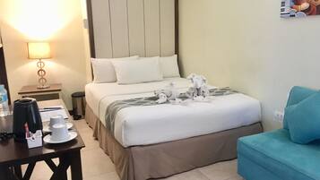 Quarto de hotel com cama, secretária com luminária, cadeira e sofá azul.