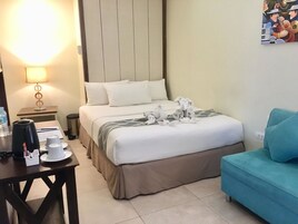 Quarto de hotel com cama, secretária com luminária, cadeira e sofá azul.