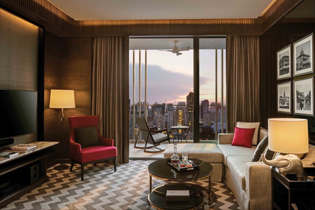 Quarto de hotel moderno com televisão grande, assentos confortáveis, mesa de centro e vista para o horizonte da cidade.