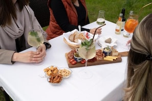 Mesa posta ao ar livre com comida, bebida e uma garrafa de vinho.