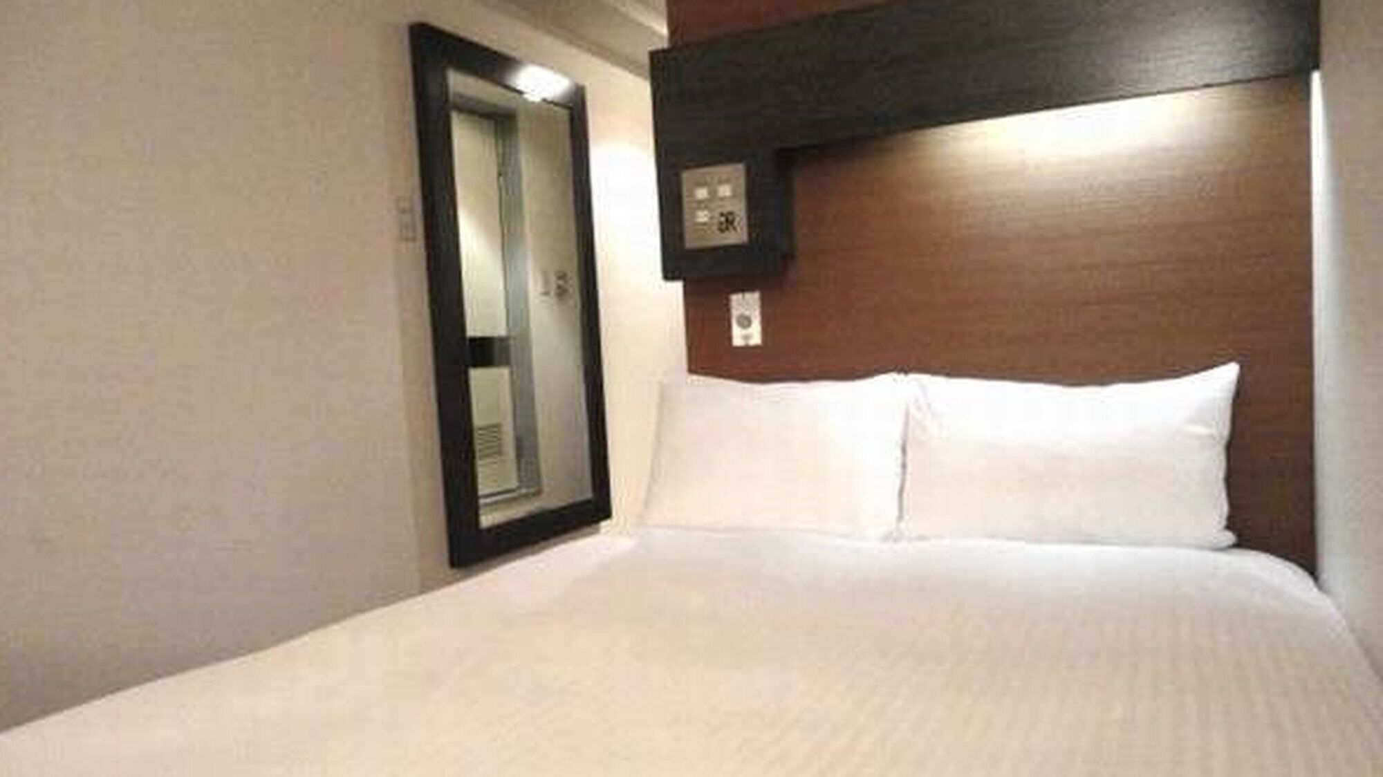 Quarto de hotel com cama, espelho e cabeceira de madeira.