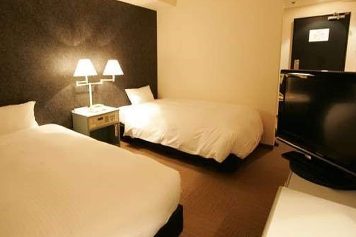 Quarto de hotel com duas camas, uma escrivaninha com abajur, uma televisão e uma porta.