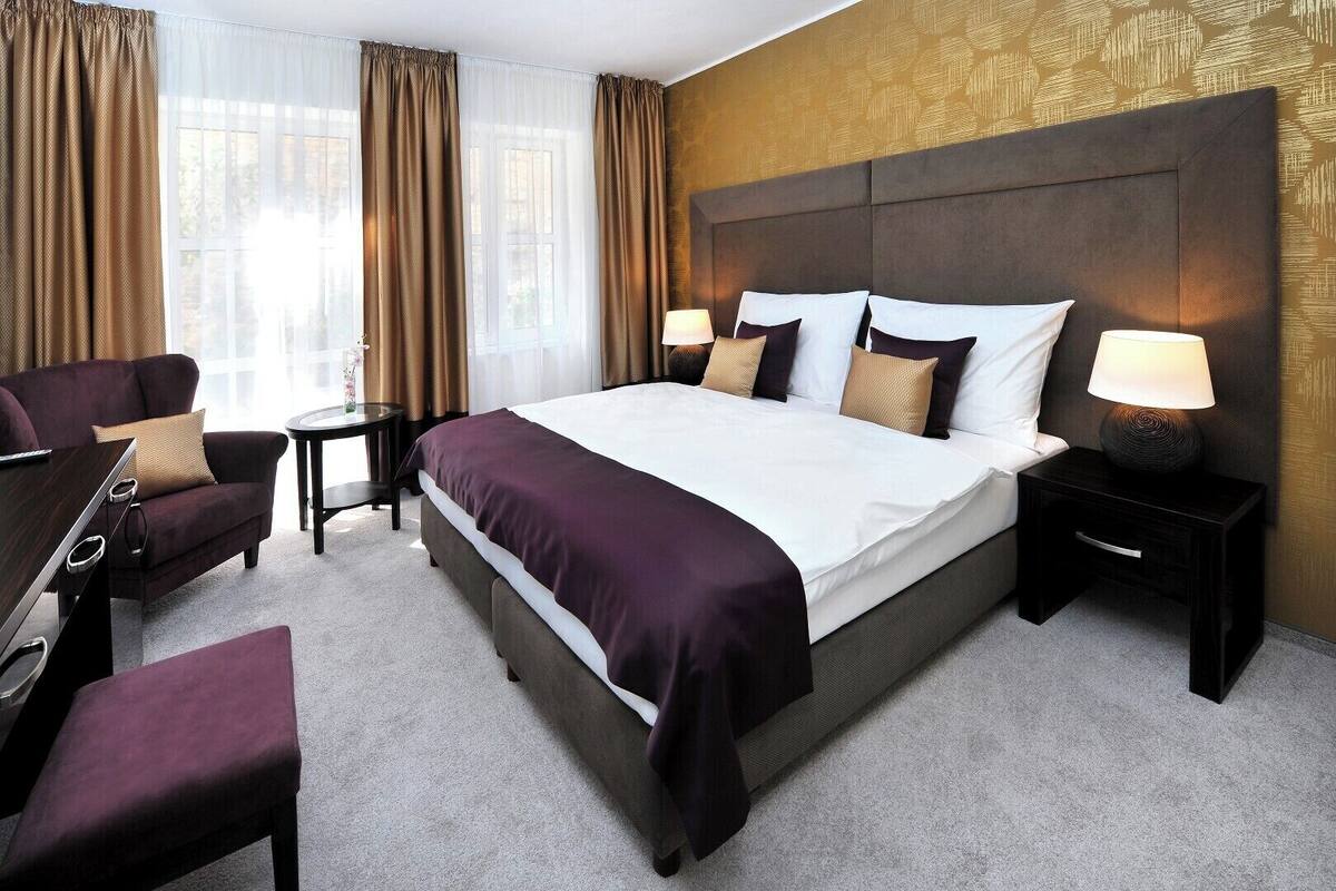 Quarto de hotel com uma cama grande, uma escrivaninha, uma cadeira e uma mesa de cabeceira com abajur.