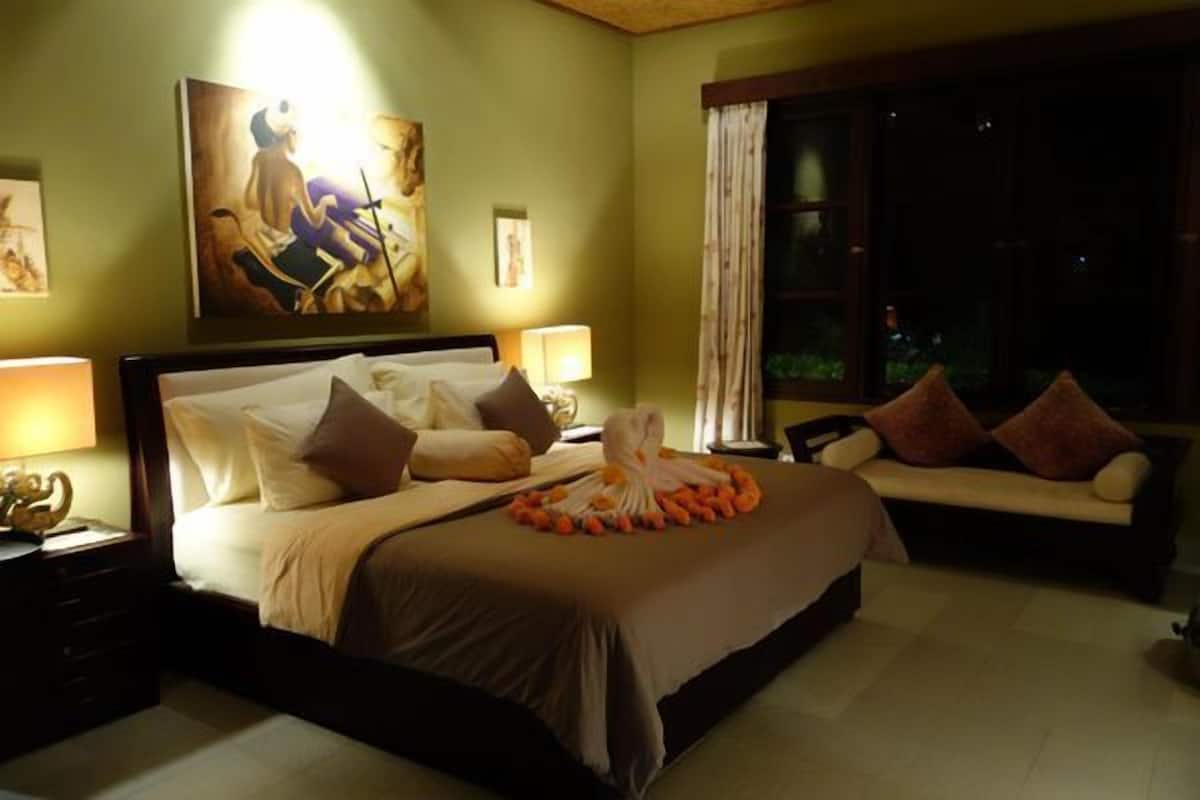 Quarto de hotel com uma cama grande, um sofá, uma mesinha de cabeceira e um quadro na parede.