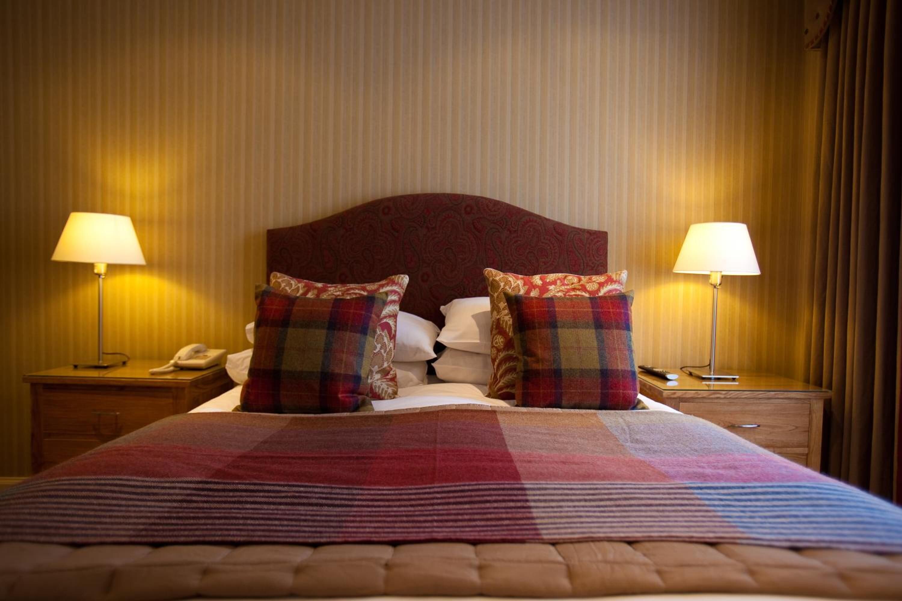Quarto de hotel com uma cama grande, duas mesas de cabeceira, um telefone e duas luminárias.