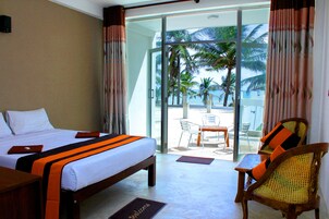 Quarto de hotel com uma cama, uma cadeira de madeira e vista para a praia e palmeiras através de uma porta de vidro.