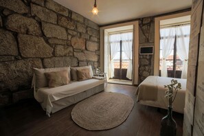 Um quarto acolhedor com parede de pedra, um sofá, uma cama e uma janela grande com cortinas.