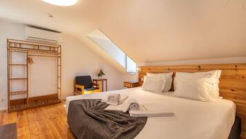 Quarto com mezanino para dormir, piso de madeira, cama com roupa de cama branca, escrivaninha e cadeira.
