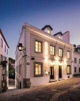 Um edifício histórico com uma placa na fachada que diz 'PENDORA', uma rua de paralelepípedos e um poste de iluminação tradicional.