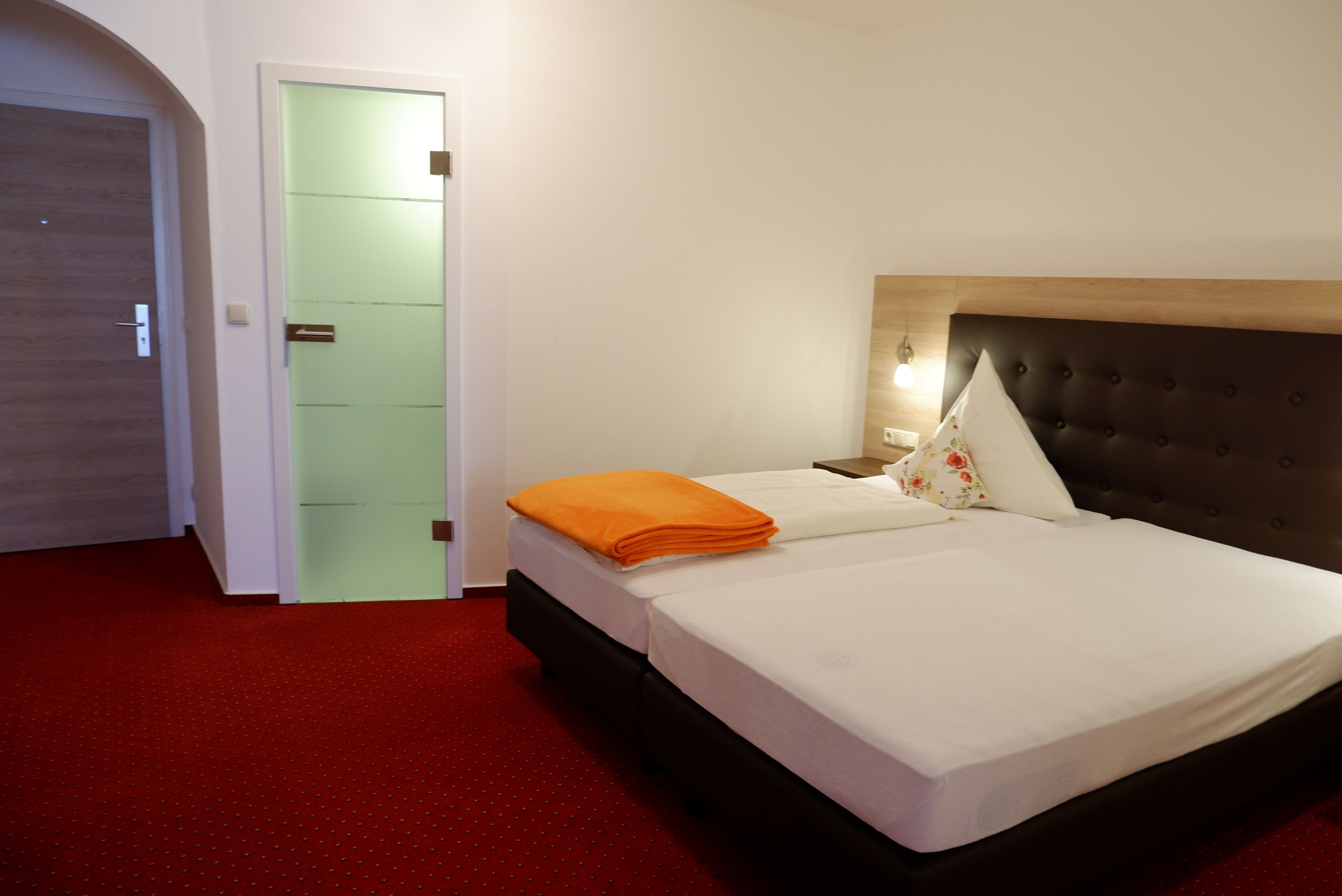 Quarto de hotel com carpete vermelho, duas camas com lençóis brancos, porta verde e cabeceira de madeira.