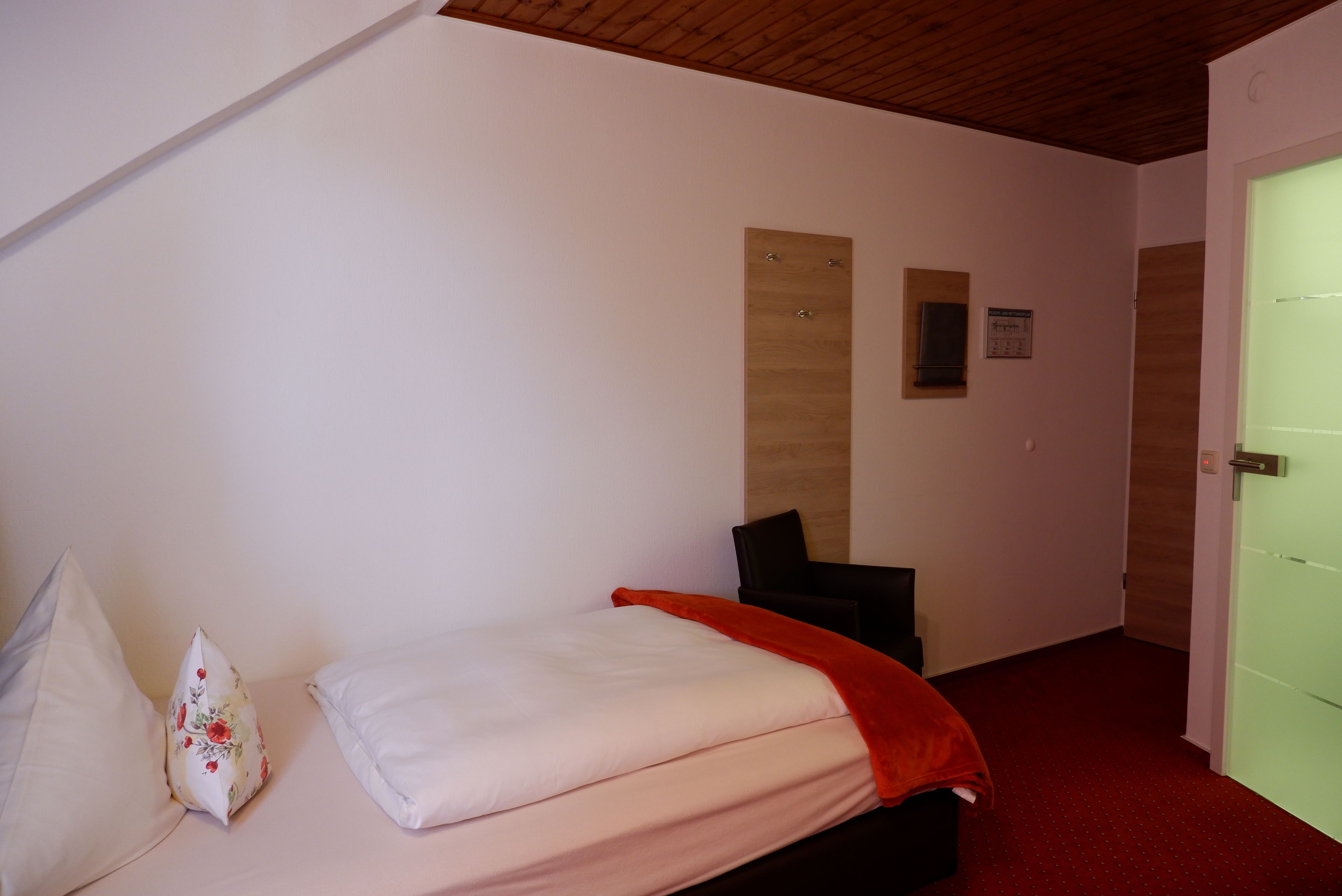Quarto de hotel com cama, cadeira, porta de madeira e painel fixado na parede.