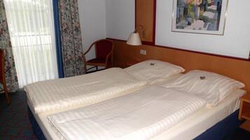 Quarto de hotel com cama de casal, uma cadeira, mesa de cabeceira, abajur e um quadro na parede.