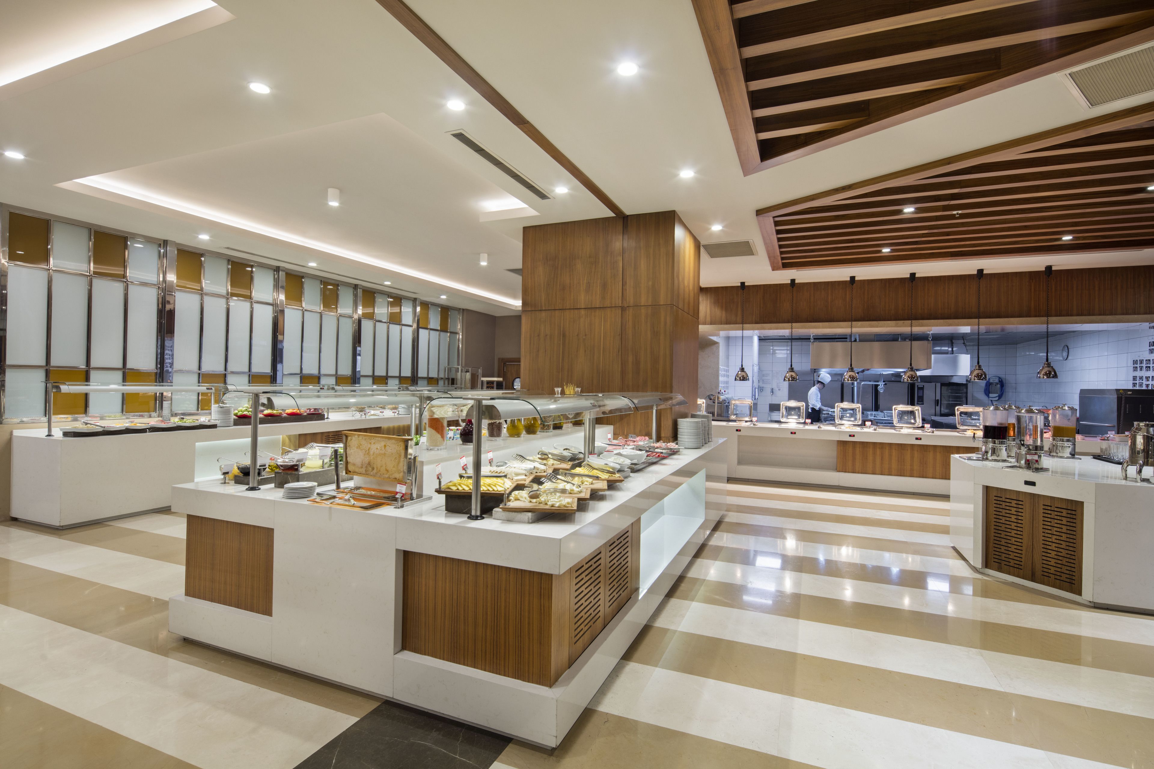 Uma área de buffet moderna com várias estações de serviço, um espaço amplo e arejado, e luminárias contemporâneas.
