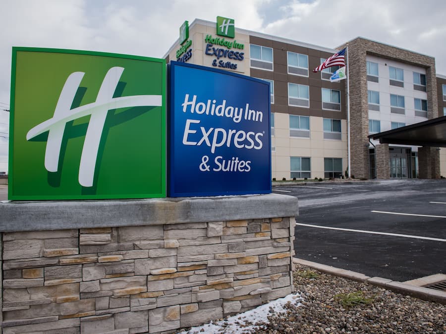 Placa do Holiday Inn Express & Suites com base de pedra, em frente a um edifício com várias janelas e uma bandeira americana.