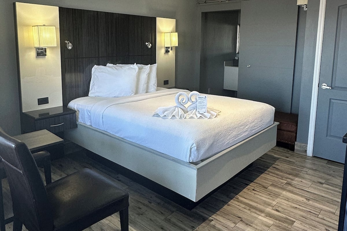 Quarto de hotel moderno com uma cama grande, mesas de cabeceira, escrivaninha e uma cadeira.