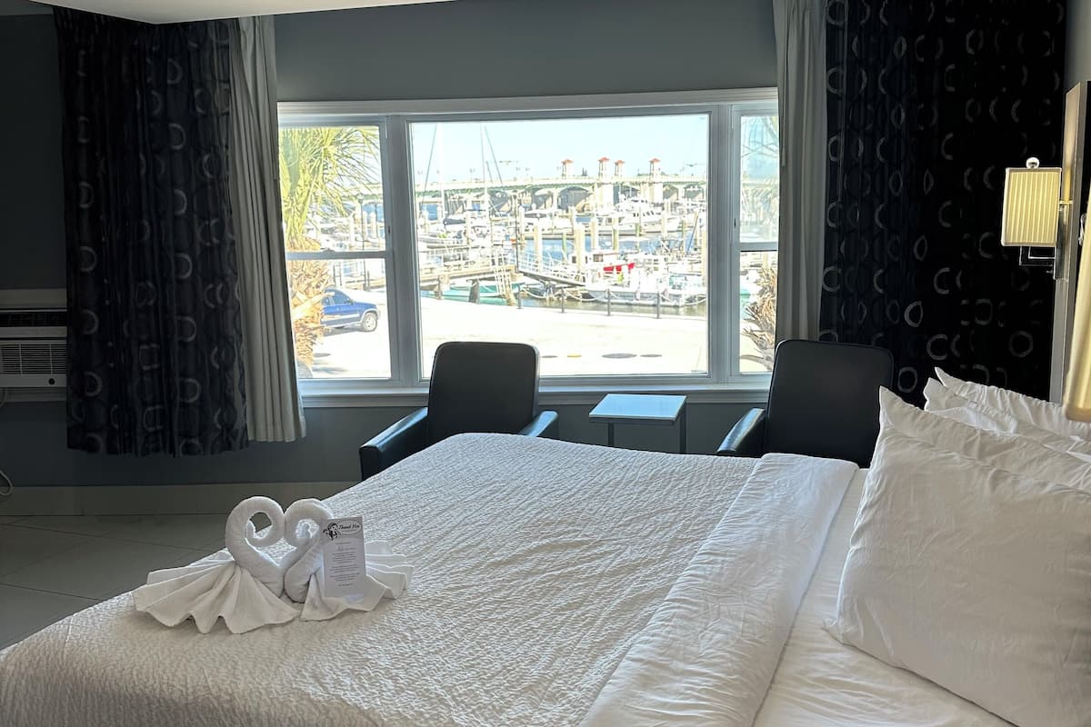 Quarto de hotel com uma cama grande, uma escrivaninha e vista para uma marina.