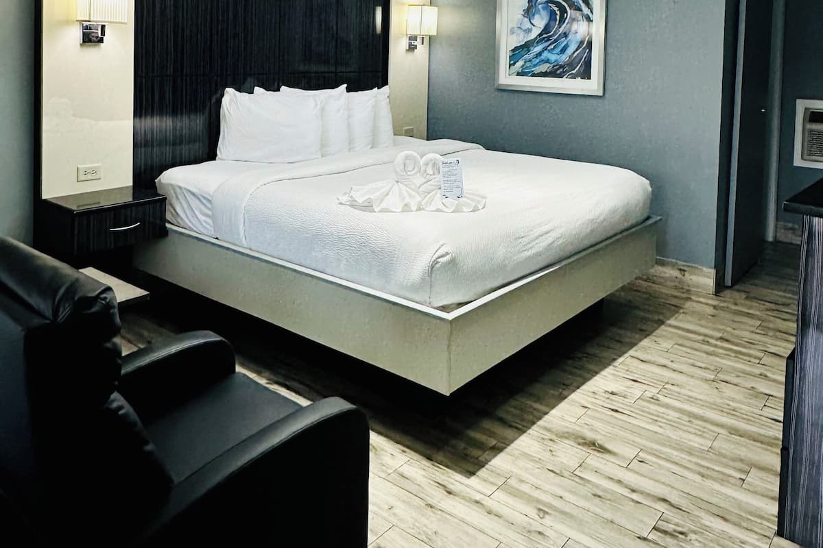 Quarto de hotel moderno com uma cama grande, abajures, um quadro na parede e piso de madeira.