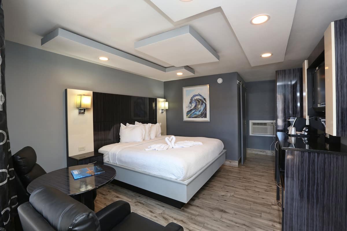 Quarto de hotel moderno com uma cama grande, uma escrivaninha, uma cadeira, um sofá, um quadro na parede e uma kitchenette.