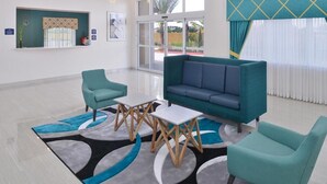 Um hall moderno com sofás azul-esverdeados, mesas brancas e tapetes estampados.