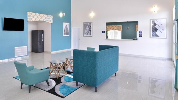 Um hall de hotel moderno com paredes verde-água, televisão de tela plana, geladeira, assentos verde-água e obras de arte nas paredes.