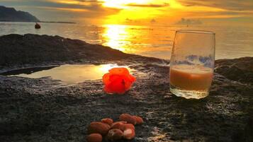 Um copo com líquido laranja sobre uma superfície rochosa, com um pôr do sol ao fundo.