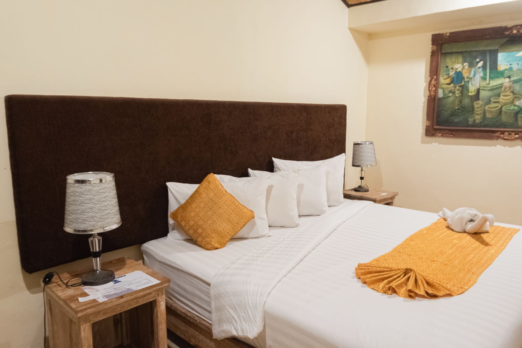 Quarto de hotel com uma cama grande, uma mesa de cabeceira de madeira, uma luminária e um quadro na parede.
