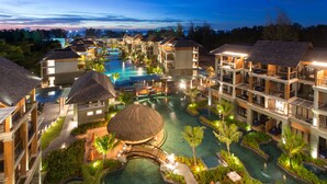 Um resort com v ários edifícios, uma piscina central e vegetação ao redor.