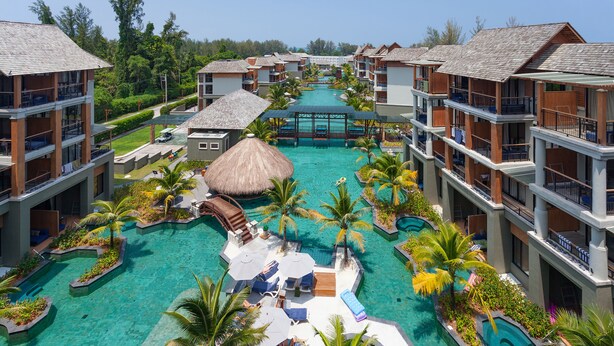 Resort com vários edifícios, uma piscina central e palmeiras ao redor.
