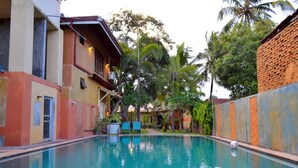 Uma piscina com superfície de água cristalina, rodeada por edifícios e palmeiras.