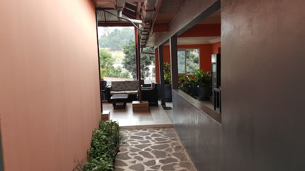 Corredor com piso de ladrilho de pedra, área de estar com sofás e uma mesa, e vista para o verde lá fora.