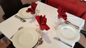 Mesa posta para quatro pessoas, com pratos brancos, talheres e guardanapos vermelhos.