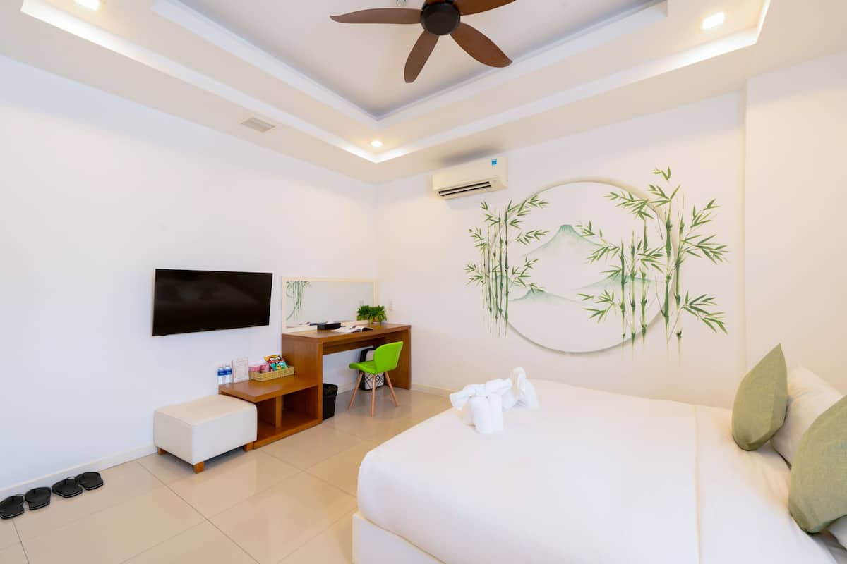 Quarto de hotel moderno com uma cama, uma escrivaninha com cadeira, televisão e ar condicionado fixado na parede.
