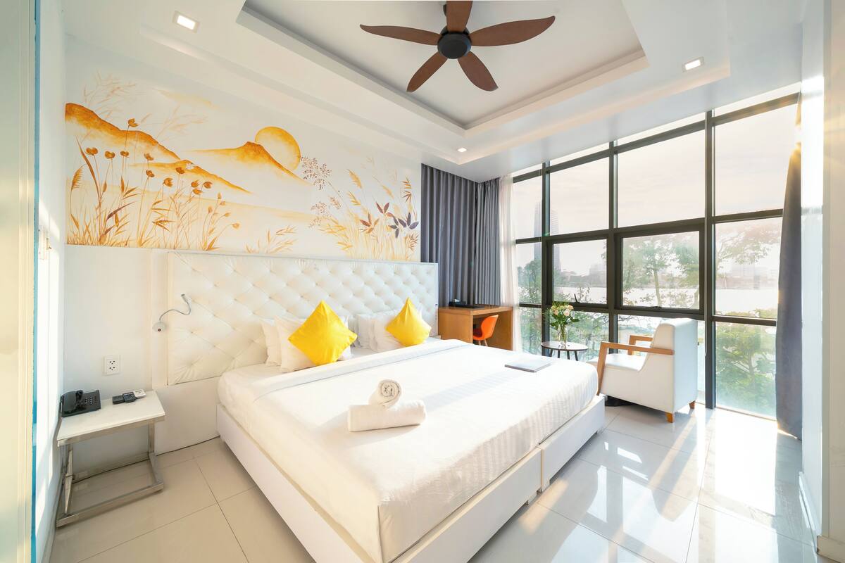 Quarto de hotel moderno com uma cama grande, uma escrivaninha e vista da cidade através de amplas janelas.