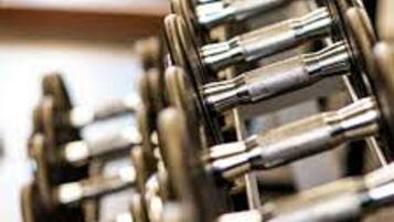 Uma fileira de equipamentos de exercício, especificamente halteres, dispostos em um ginásio.