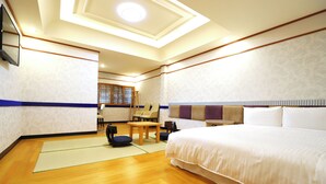 Quarto de hotel com uma cama grande, piso de madeira, uma mesa pequena e cadeiras.