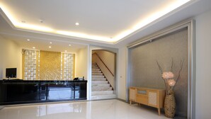 Um hall amplo com balcão de recepção, escada e um vaso decorativo.