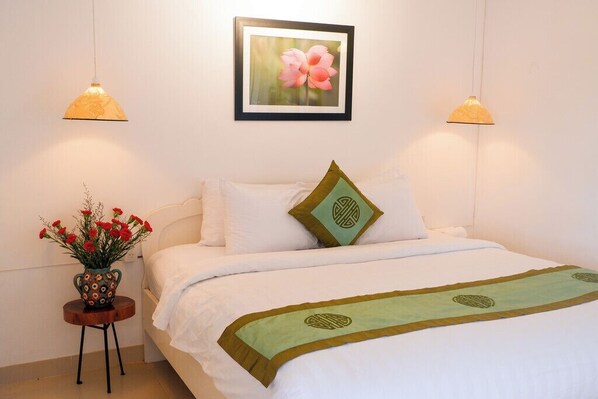 Cama bem arrumada com lençóis brancos e um corredor decorativo verde, uma obra de arte floral emoldurada acima da cama, e duas luminárias fixadas na parede.