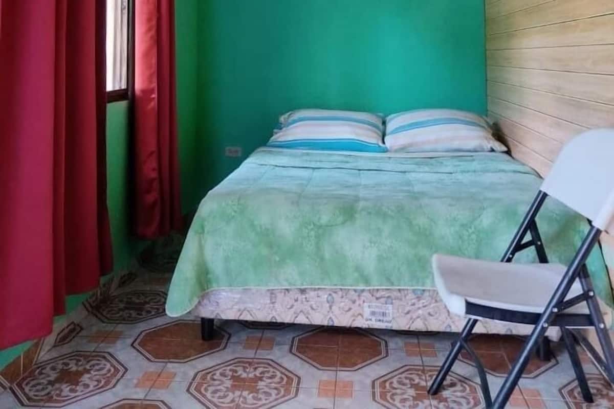 Quarto pequeno com uma cama de solteiro, parede verde, teto de madeira e piso estampado.