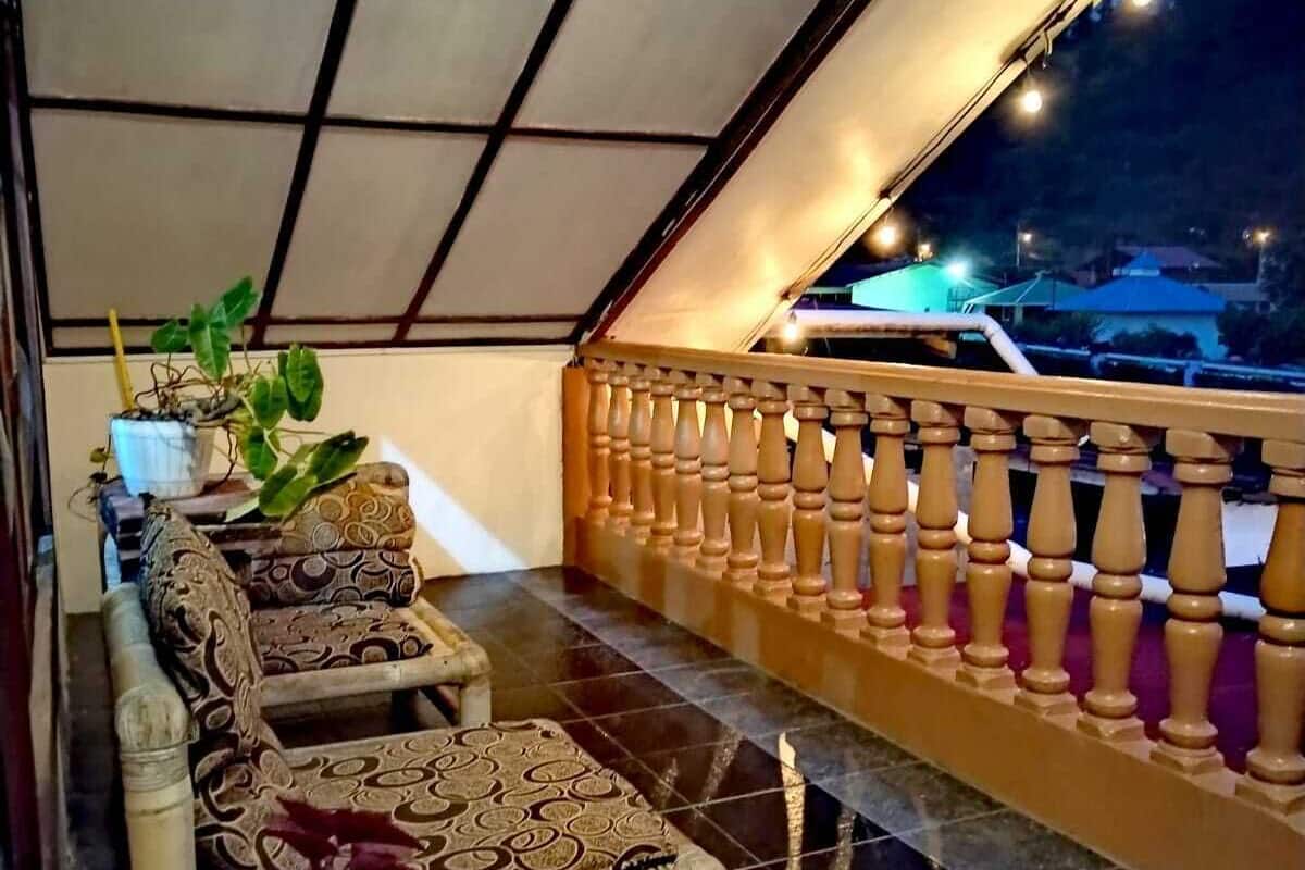 Uma varanda com sofá, cadeiras, guarda-corpo e plantas em vasos.