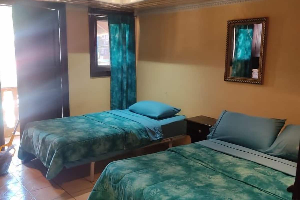 Quarto com duas camas, janela com cortinas, espelho na parede e chão de azulejos.