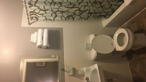 Casa de banho com cortina de chuveiro, sanita, lavatório e suporte para toalhas.