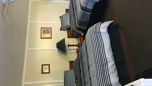 Quarto com cama, travesseiros, mesa de cabeceira, luminária e quadros nas paredes.