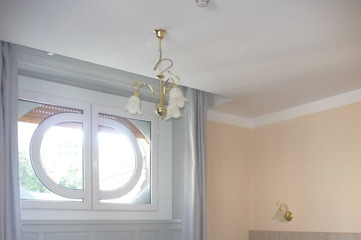 Quarto com cama, janela com cortinas, lustre e luminária na parede.