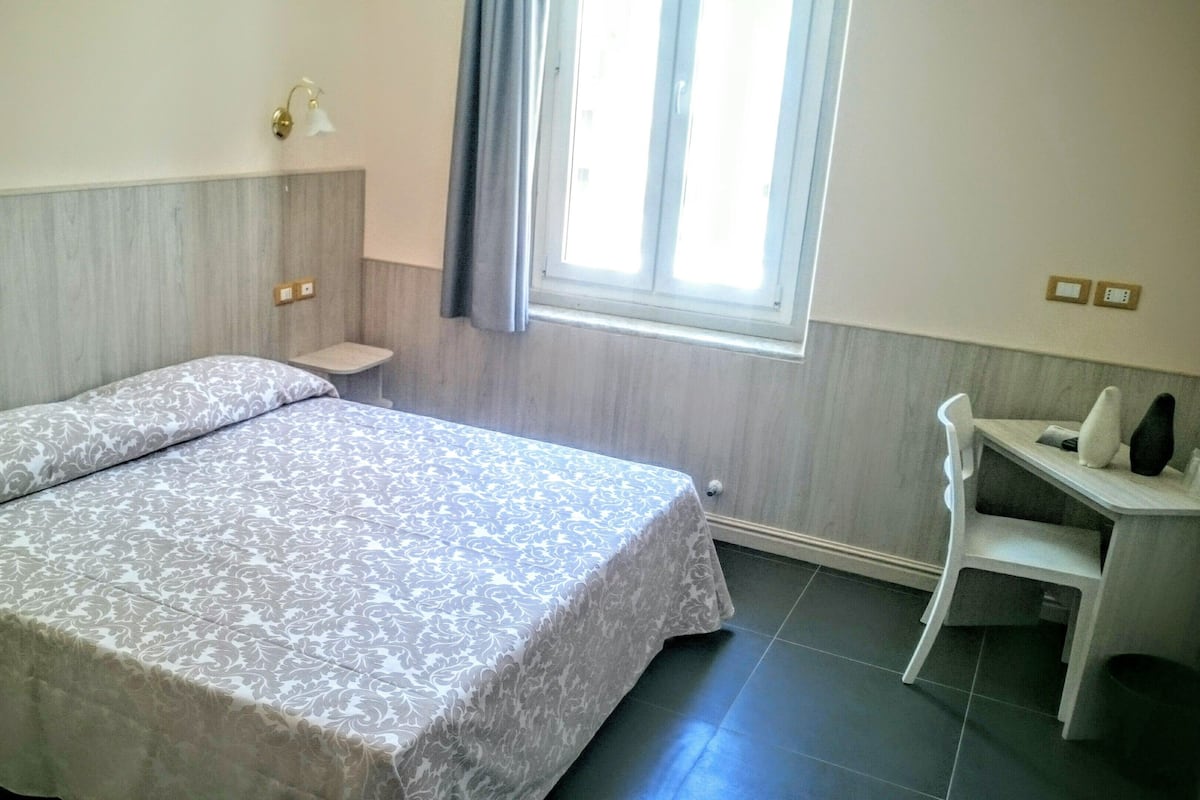 Um quarto com uma cama, uma mesa e uma janela.