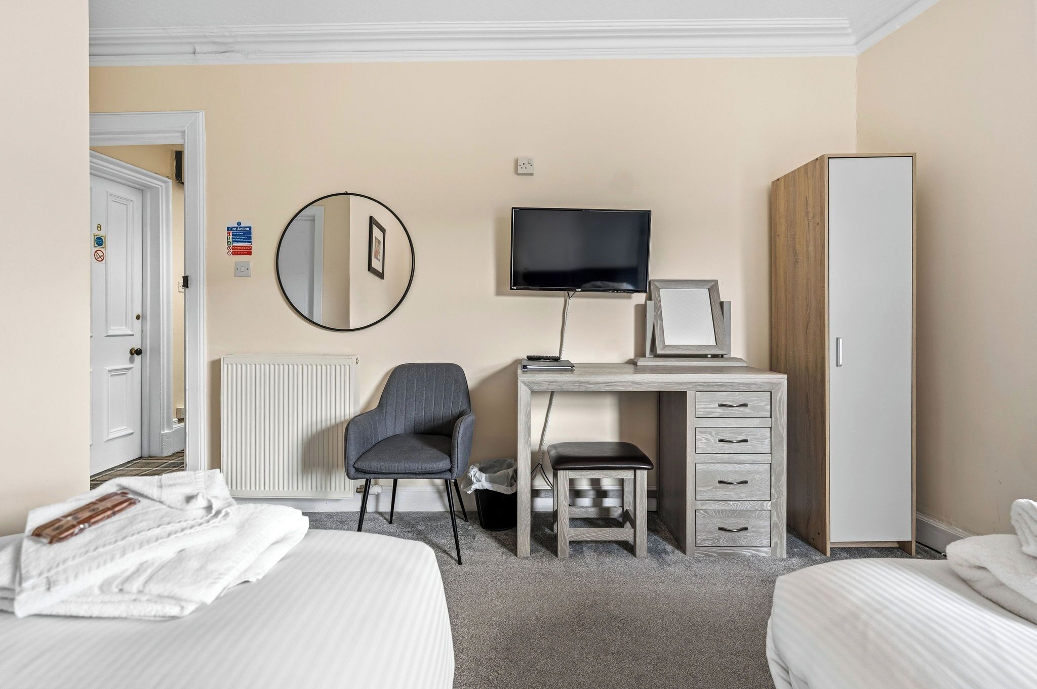 Quarto de hotel com cama, secretária com computador, cadeira, guarda-roupa e espelho.