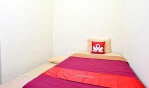 Quarto pequeno, com uma cama de solteiro, um edredom vermelho e bege e um travesseiro vermelho com um símbolo de lótus branco.