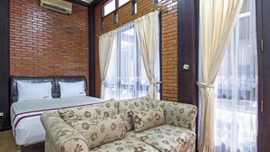 Quarto de hotel com cama, sofá, parede de tijolos e janela com cortinas.