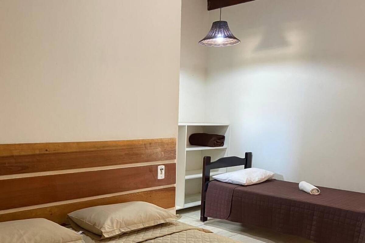 Um quarto pequeno e acolhedor, com cabeceira de madeira, uma cama de solteiro com colchão acolchoado, uma pequena mesinha de cabeceira e um pendente.