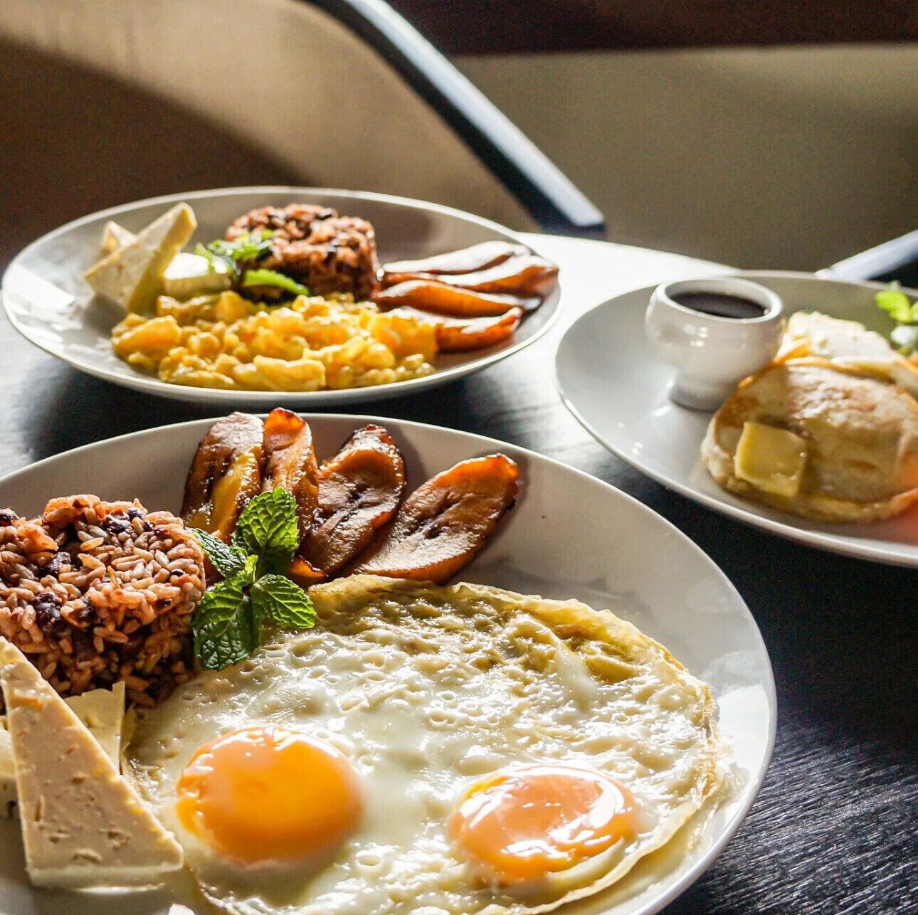 Uma mesa com três pratos de comida de café da manhã, incluindo ovos, bacon e arroz.